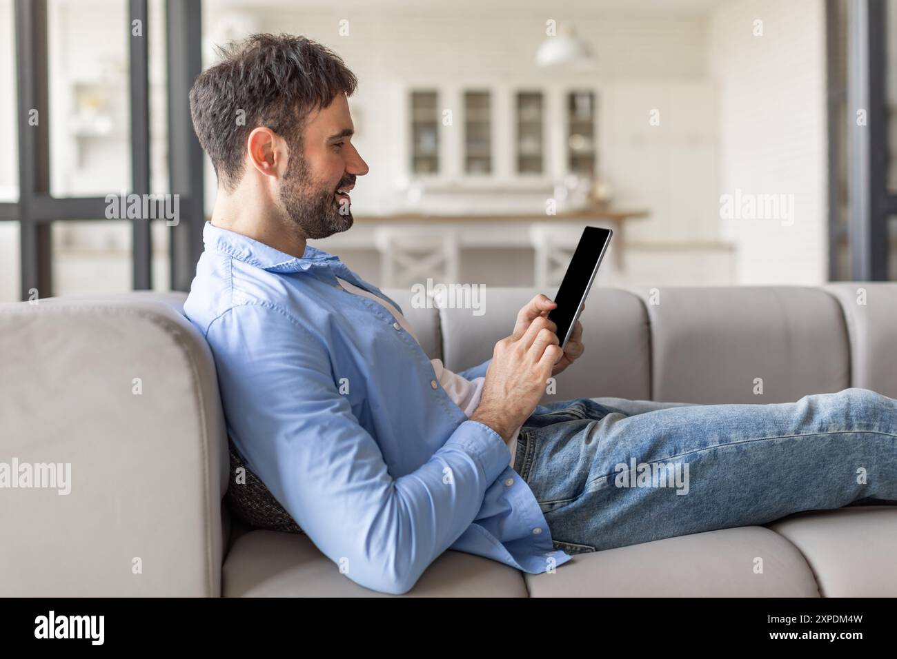 Man Using Tablet on a Couch in a Modern Home Stock Photo - Alamy