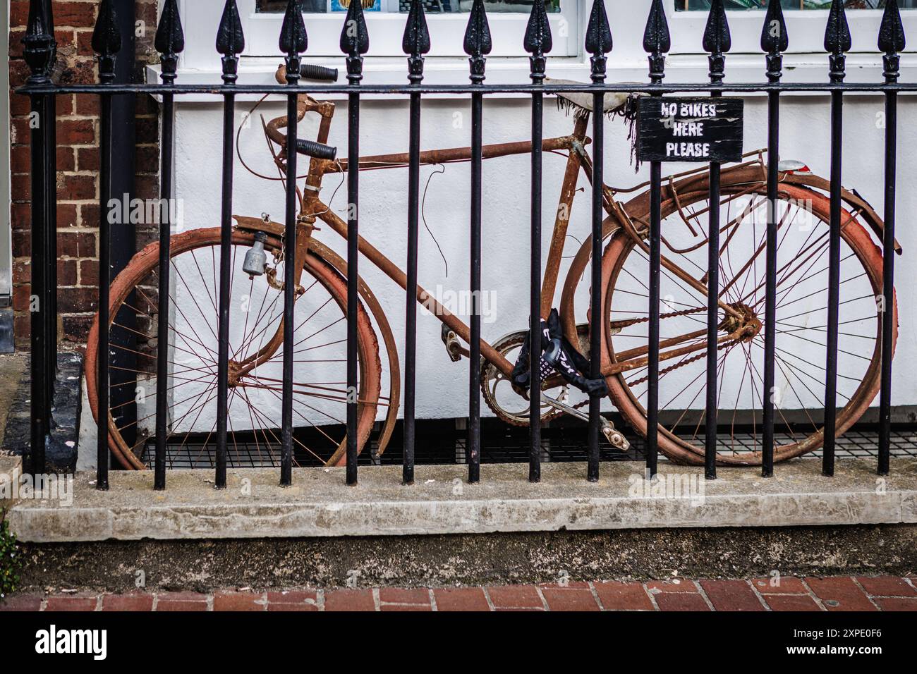 A corroded bicycle chained to railings by a "no bikes here please" sign ...