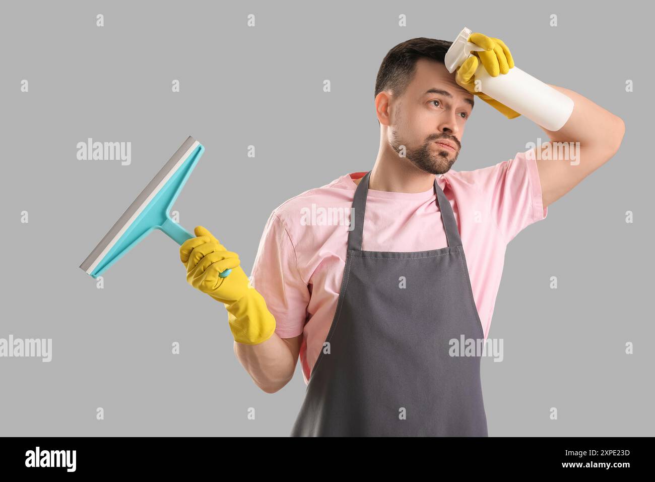 Tired male janitor with squeegee and detergent on grey background Stock ...