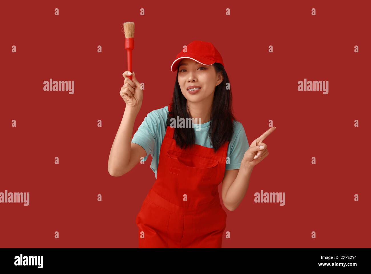 Female Asian painter with brush pointing at something on red background ...