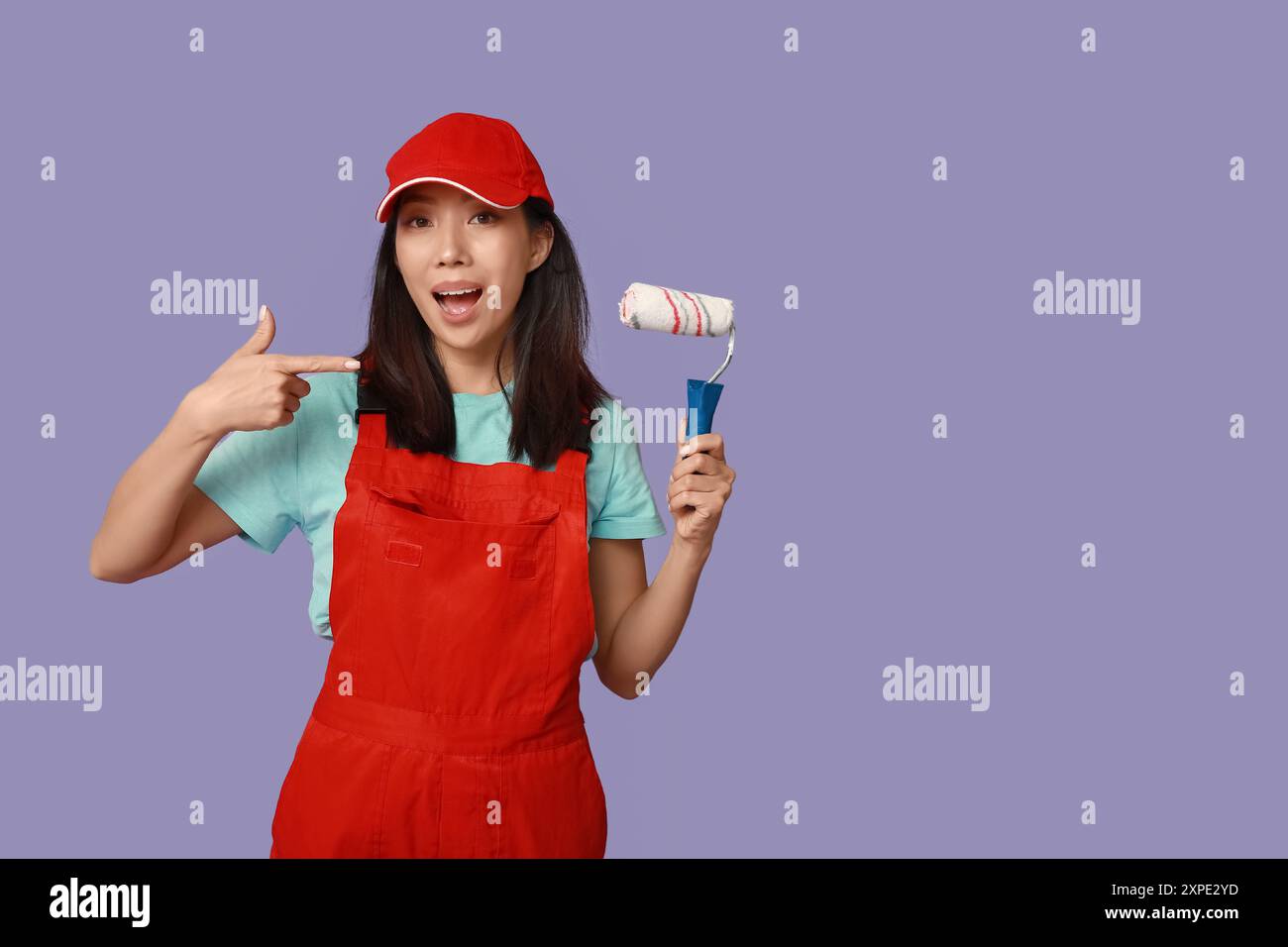 Female Asian shocked painter pointing at roller on purple background ...