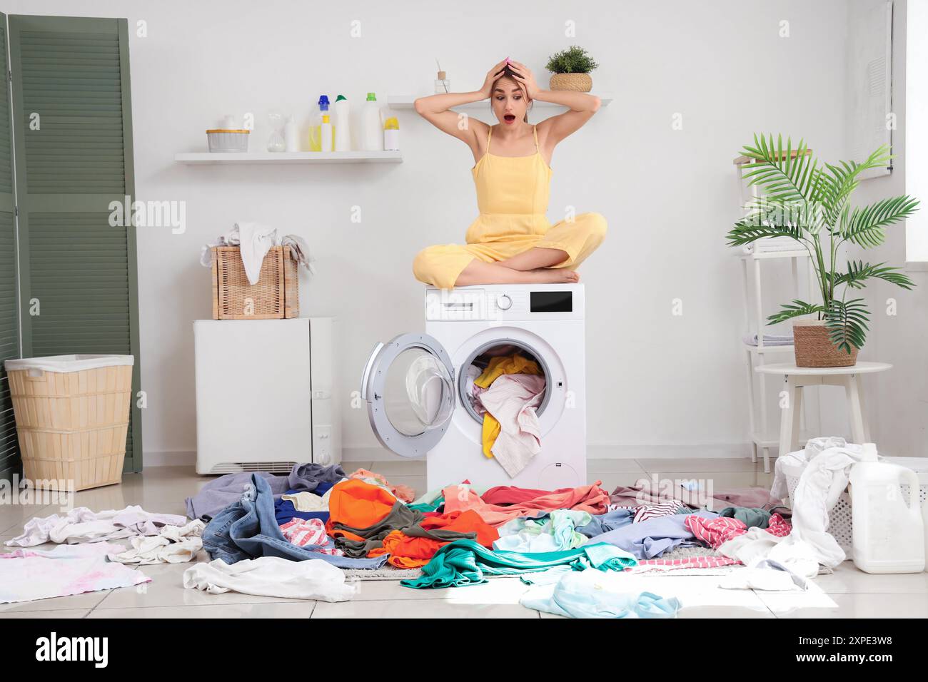 Shocked young woman sitting on washing machine with piles of dirty ...