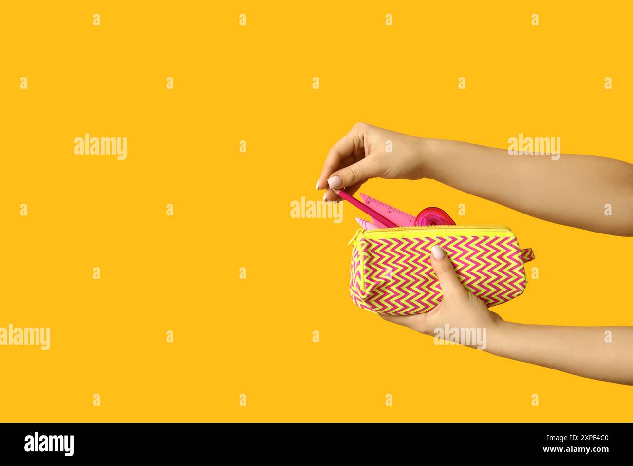 Female hands holding pencil case with stationery on yellow background ...