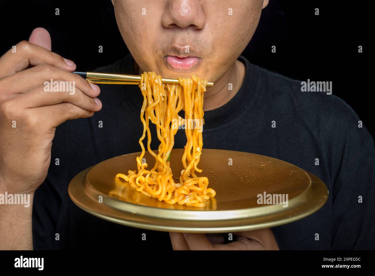 A man is eating instant noodles with chopsticks. The noodles are long ...