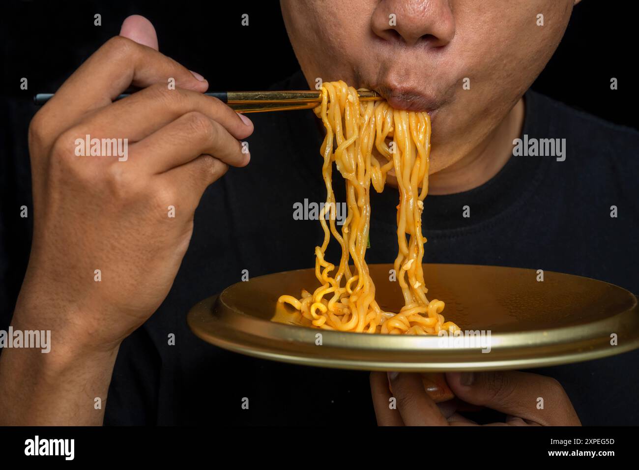 A man is eating instant noodles with chopsticks. The noodles are long ...