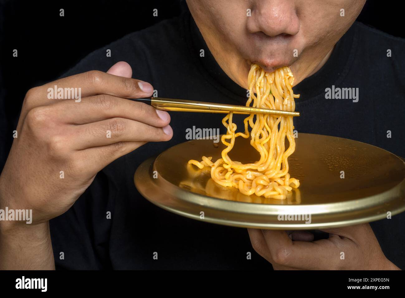 A man is eating instant noodles with chopsticks. The noodles are long ...