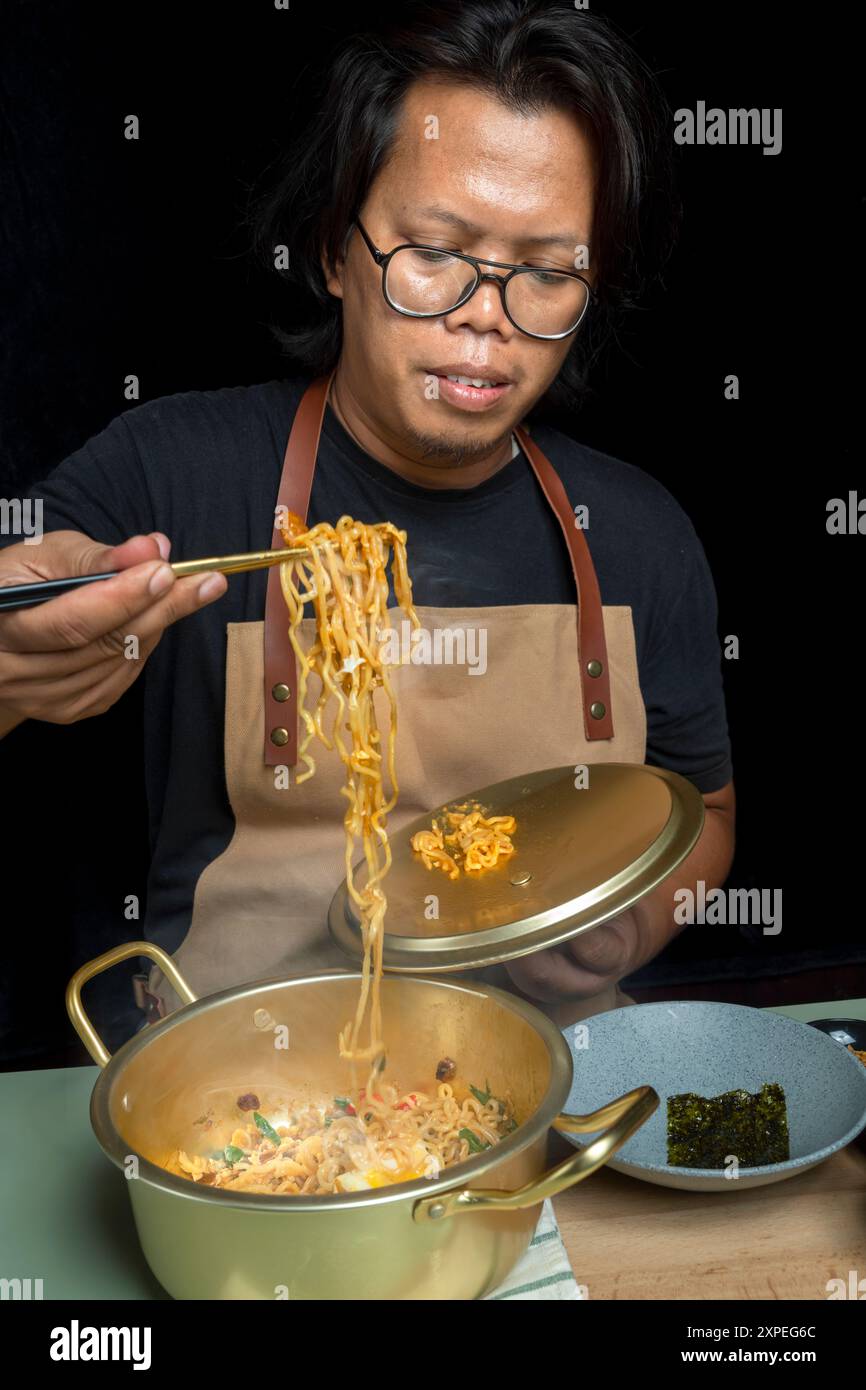 A man is eating instant noodles with chopsticks. The noodles are long ...