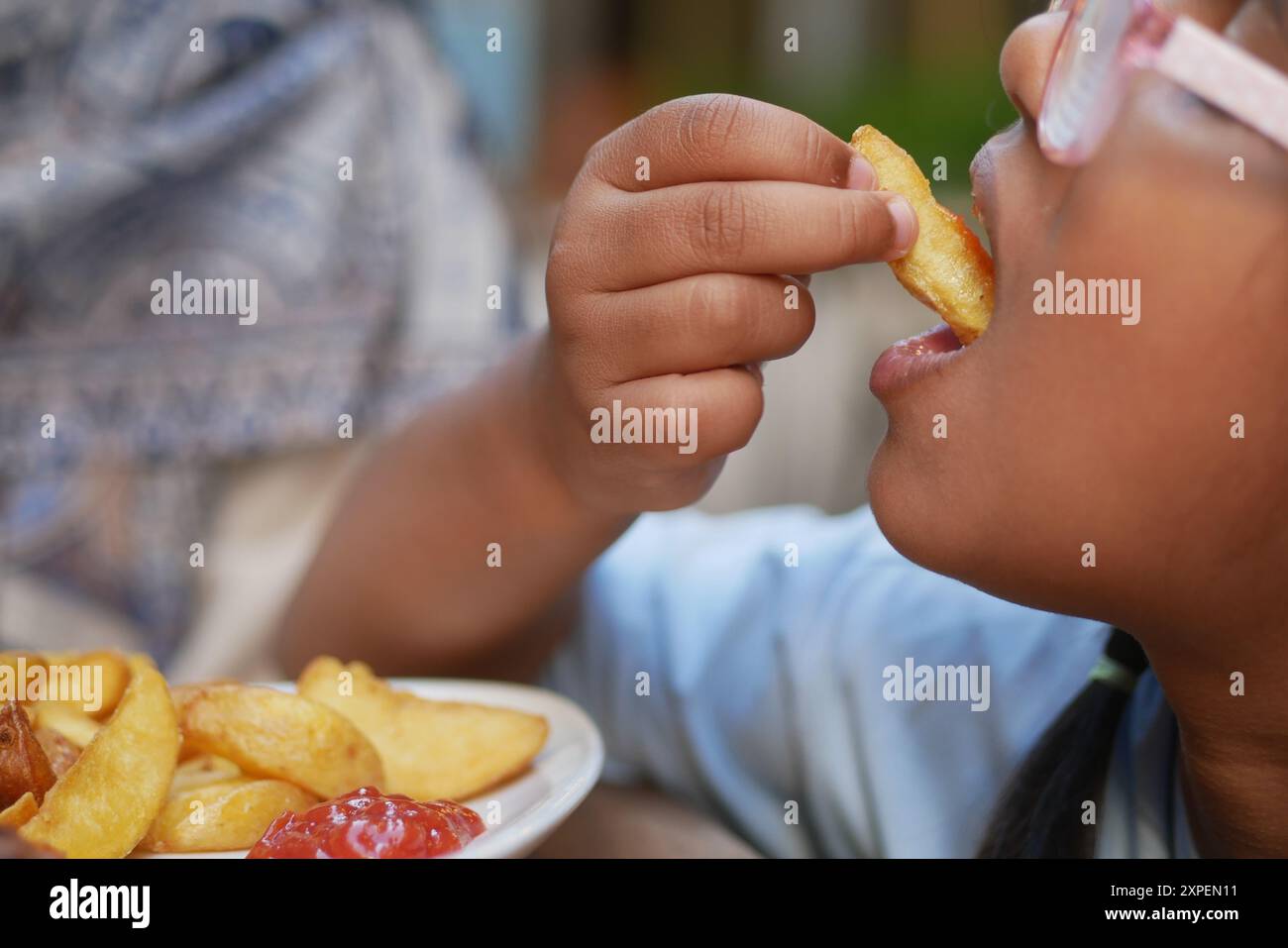 A cheerful child joyfully eating crispy fries with ketchup outdoors ...