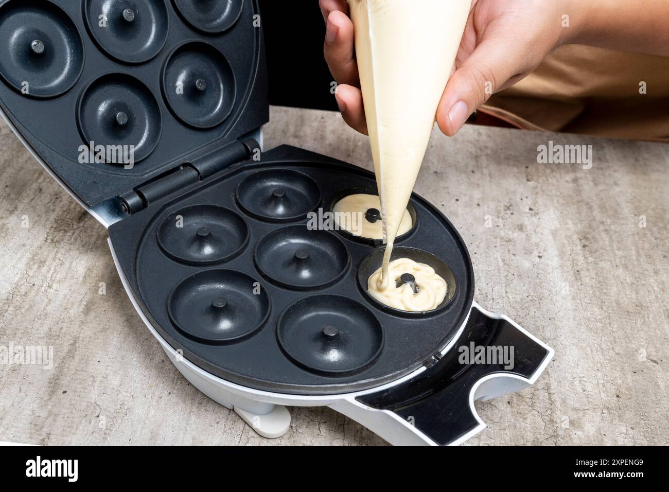 A person is making donuts in a donut maker. The donuts are being filled ...