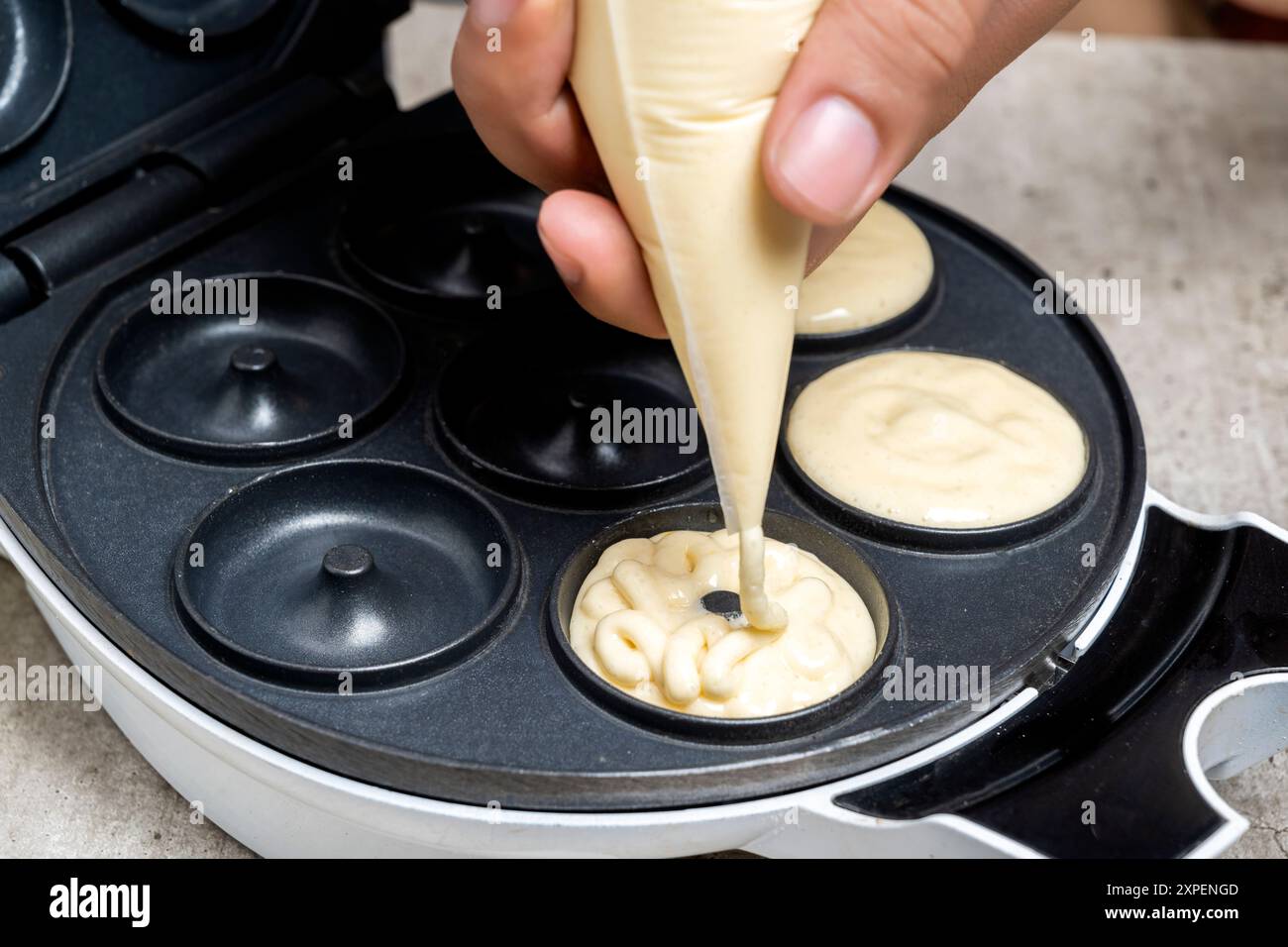 A person is making donuts in a donut maker. The donuts are being filled ...