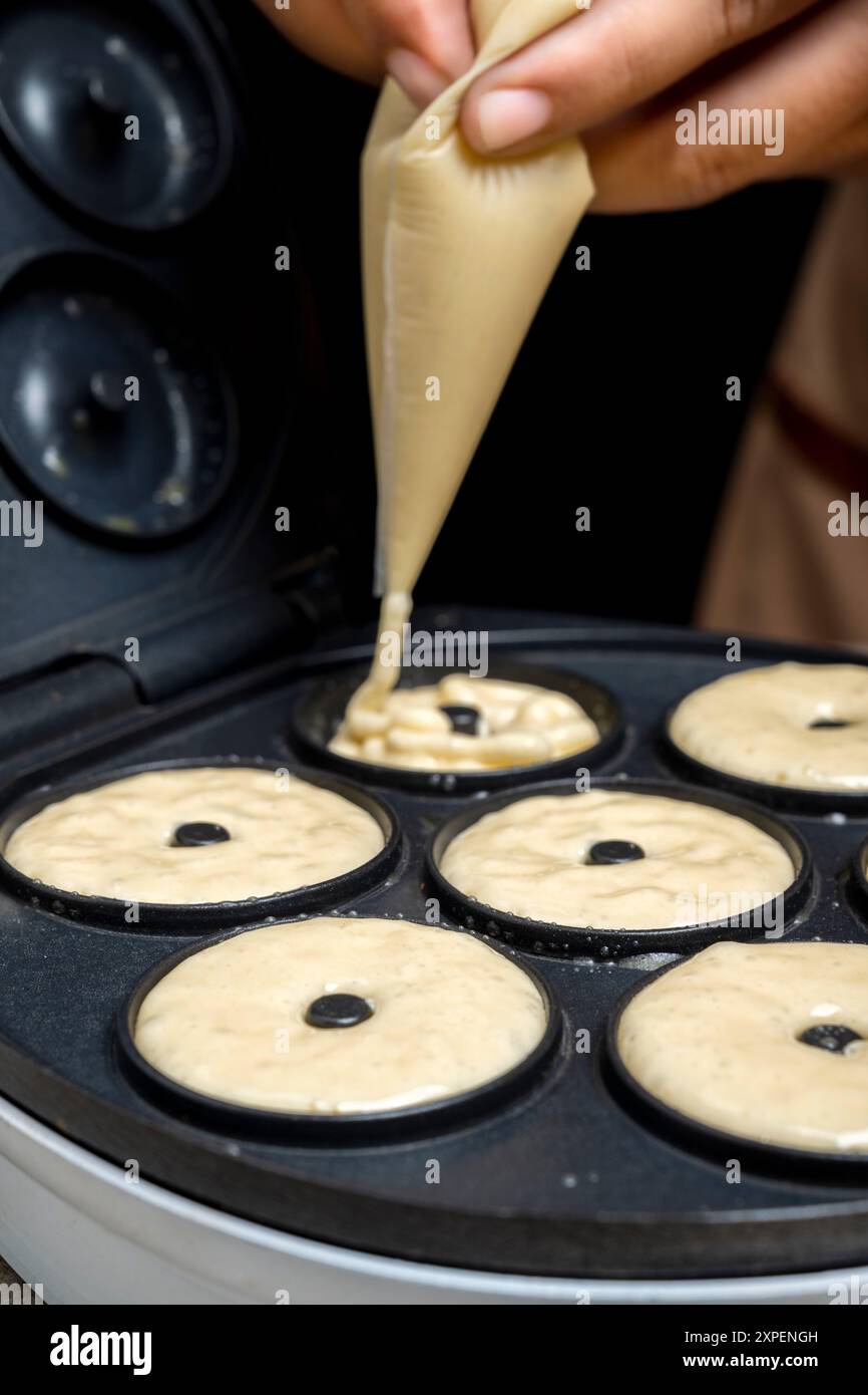 A person is making donuts in a donut maker. The donuts are being filled ...