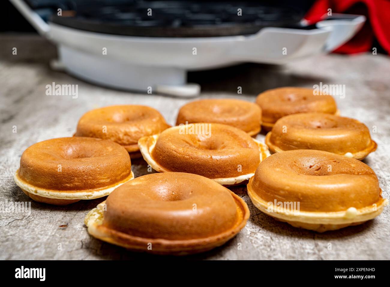 A donut pan sits on a counter next to a donut maker. There are six ...