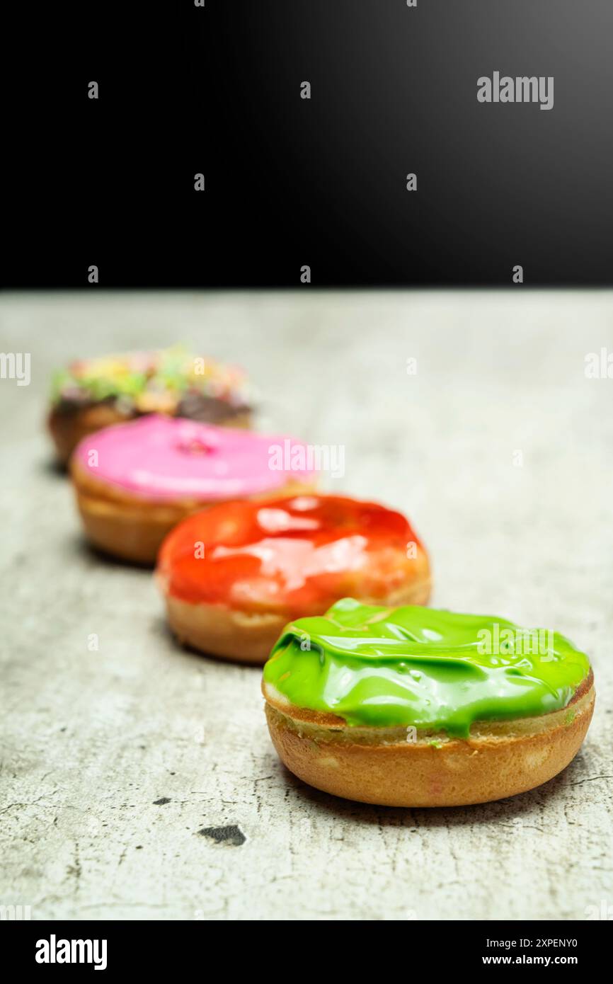 Four donuts with different colors and flavors are arranged in a row on ...