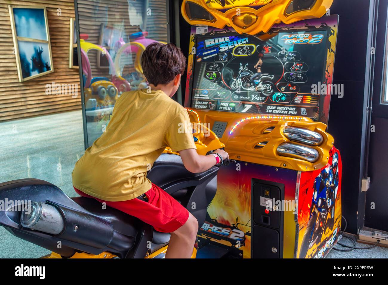 A boy playing a motorcycle racing video game at the amusements arcade ...