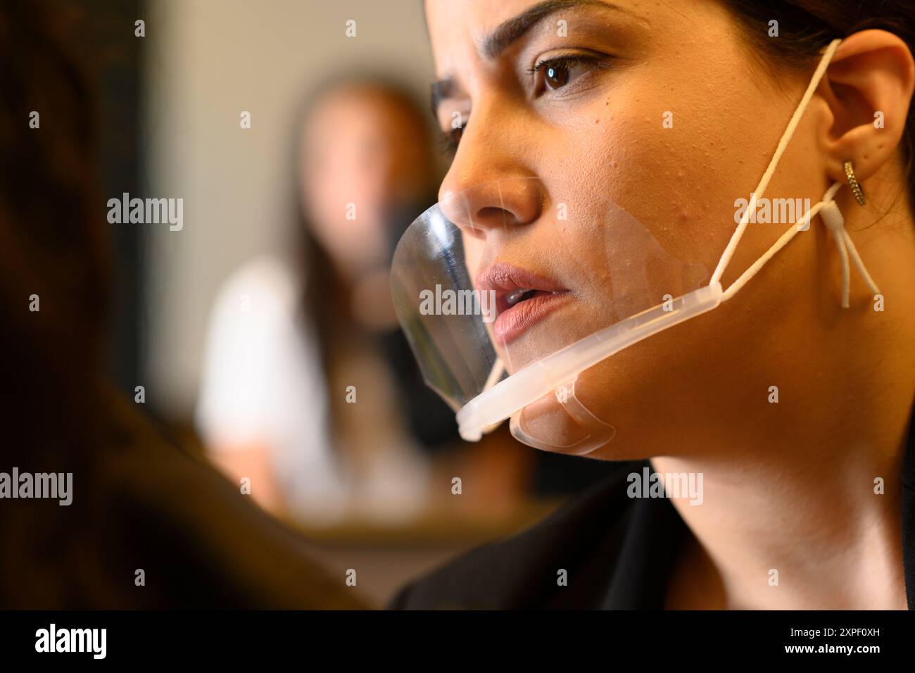 Focused businesswoman in an office wears a clear face mask, talking ...