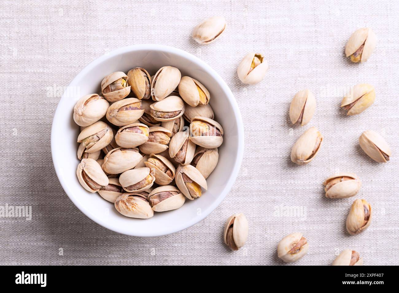 Pistachios in their shells, roasted and salted, in white bowl on linen. Crunchy roasted fruits ...