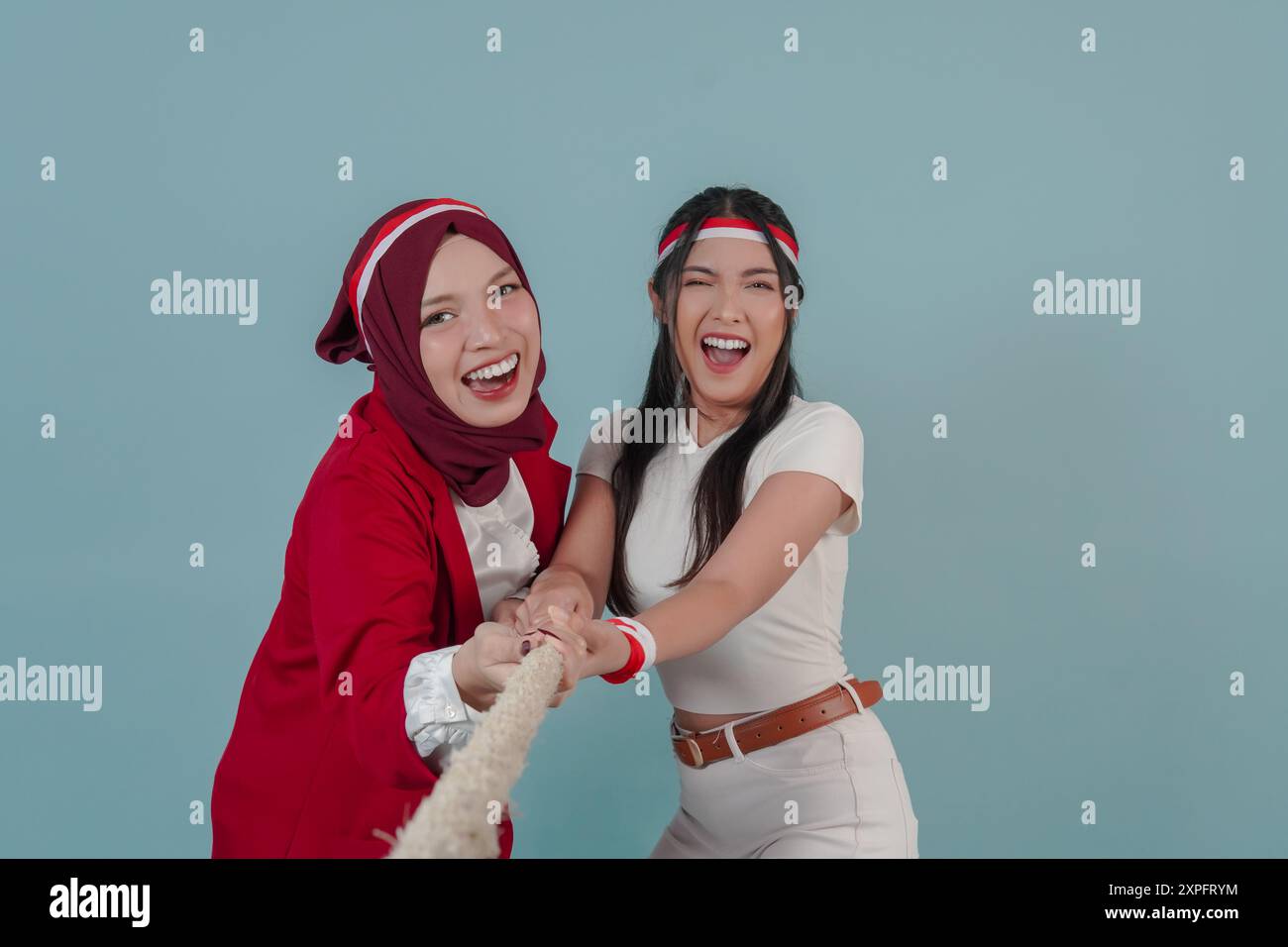 Two cheerful Indonesian woman wearing flag headband are pulling on a ...
