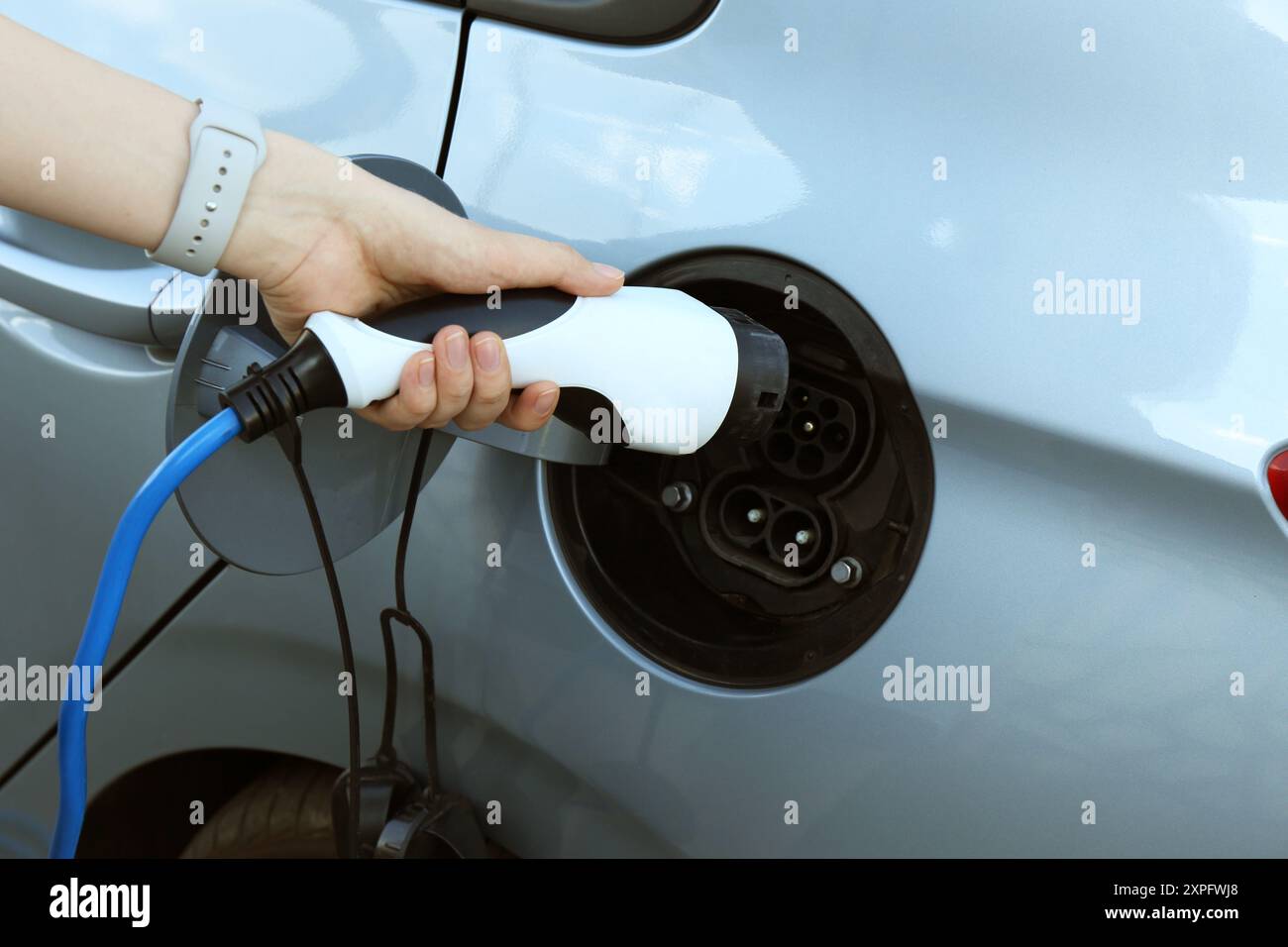 Woman inserting plug into electric car socket at charging station ...