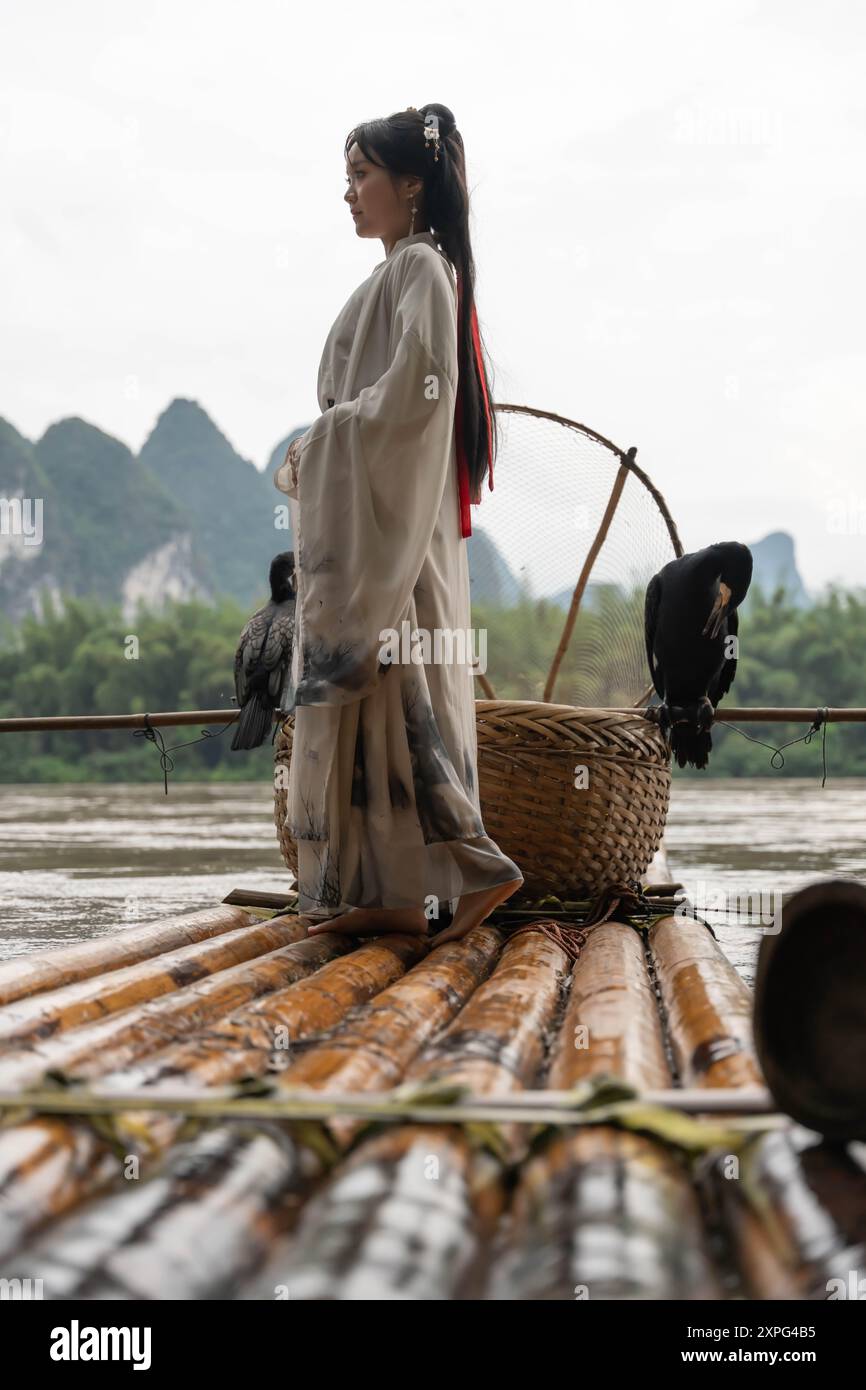 Young Chinese Hanfu woman looking down at bamboo raft by Li River in ...