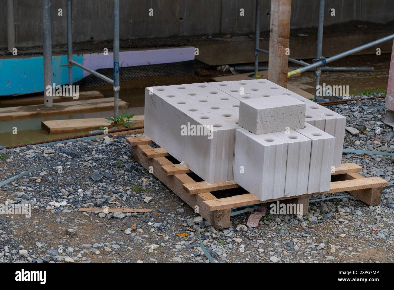 A pallet stacked with concrete blocks rests on gravel at a construction ...