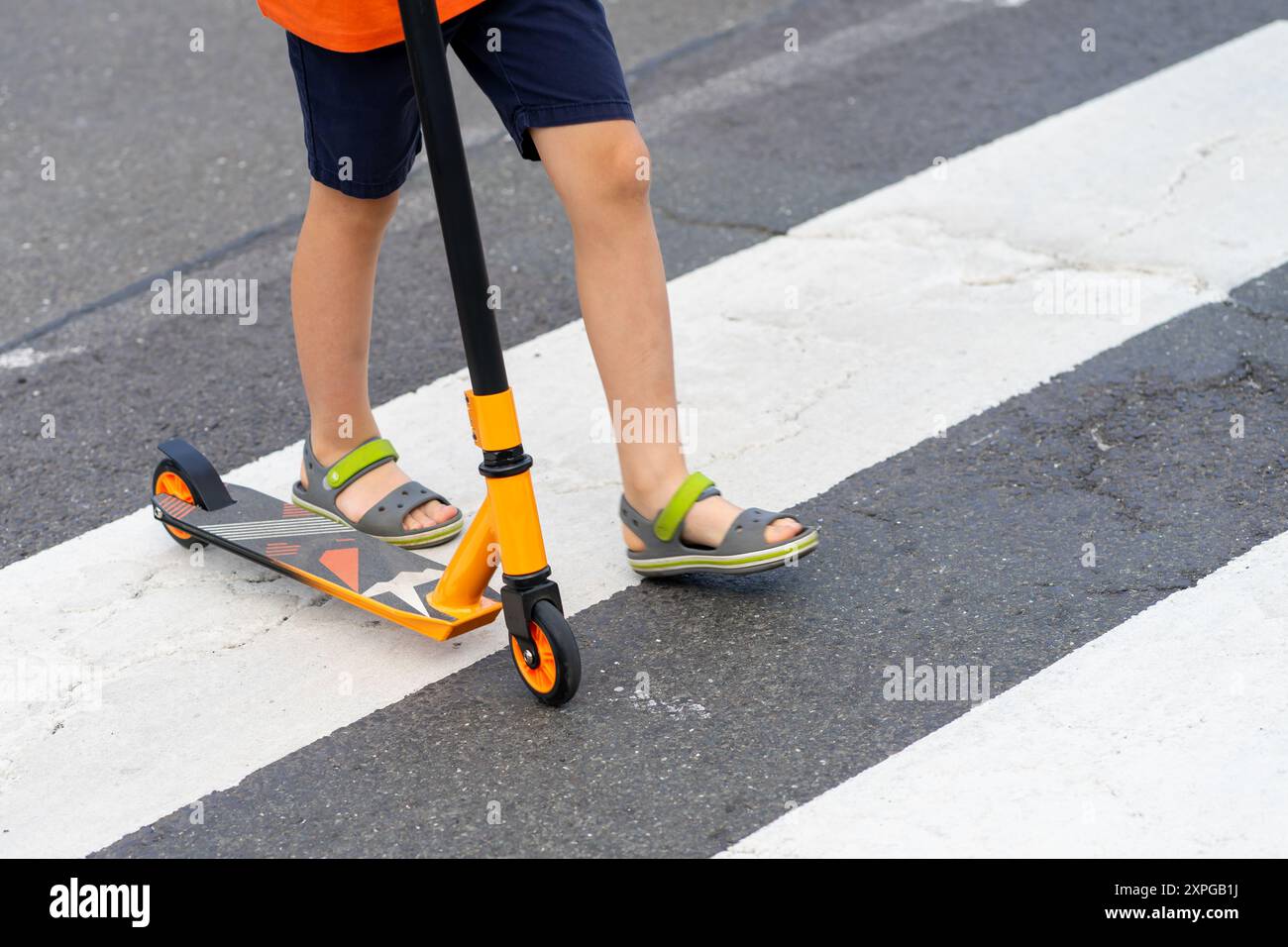A child on a scooter walks along a pedestrian crossing Stock Photo - Alamy