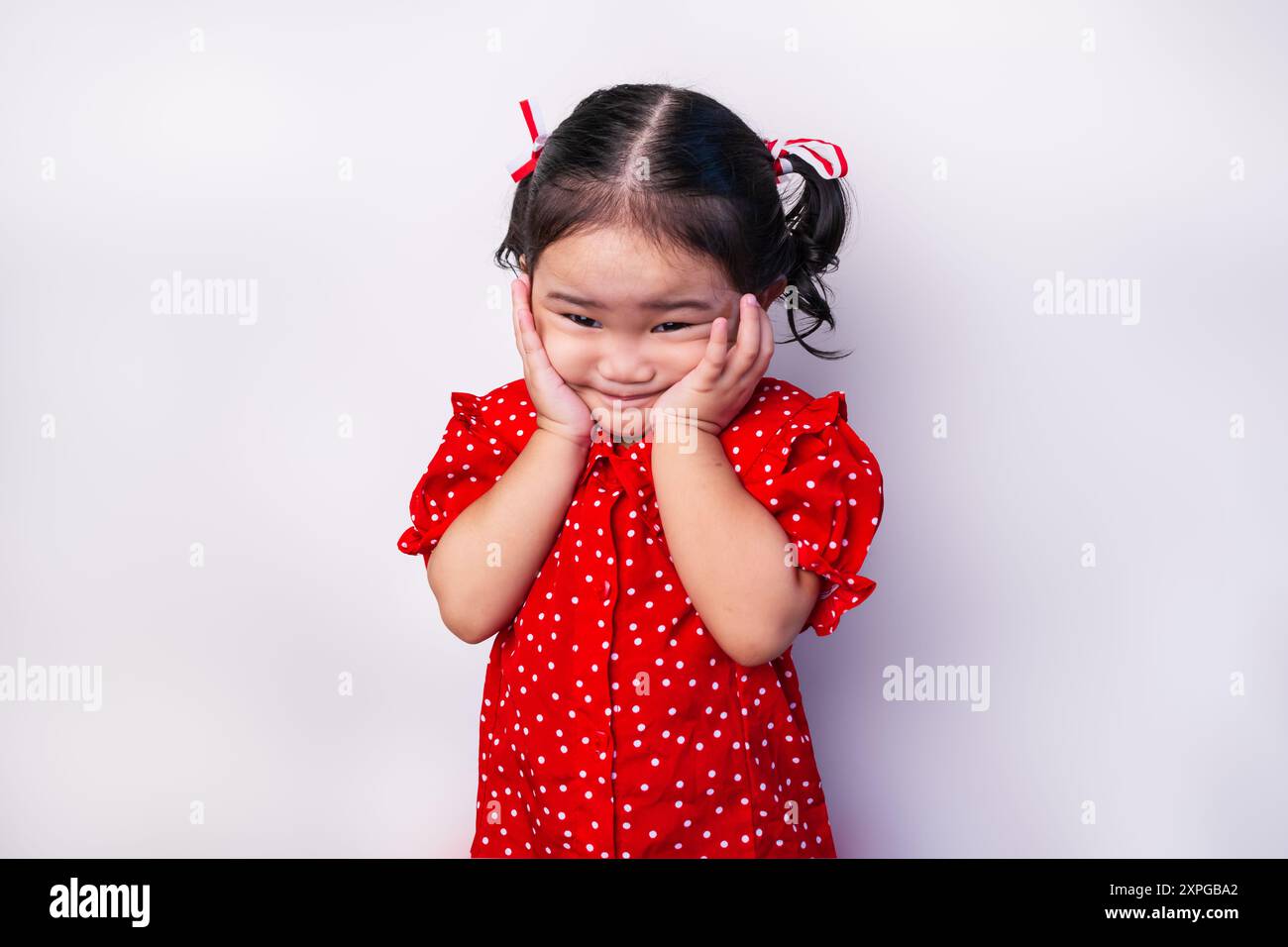 Asian toddler girl, smiling with both hands on cheeks, wearing a red ...