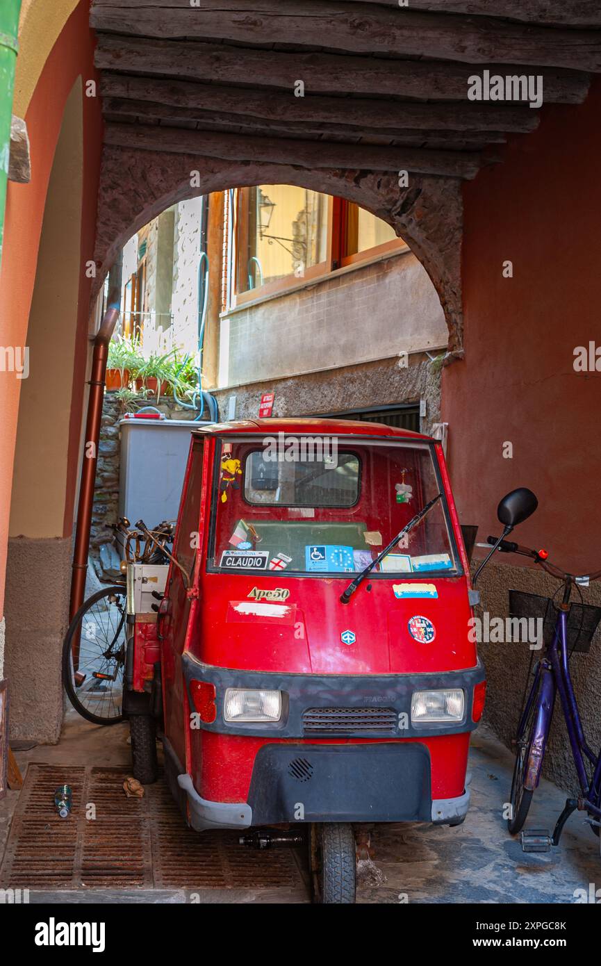 Scenic view of a small red three-wheeled car under a gate in an italian ...