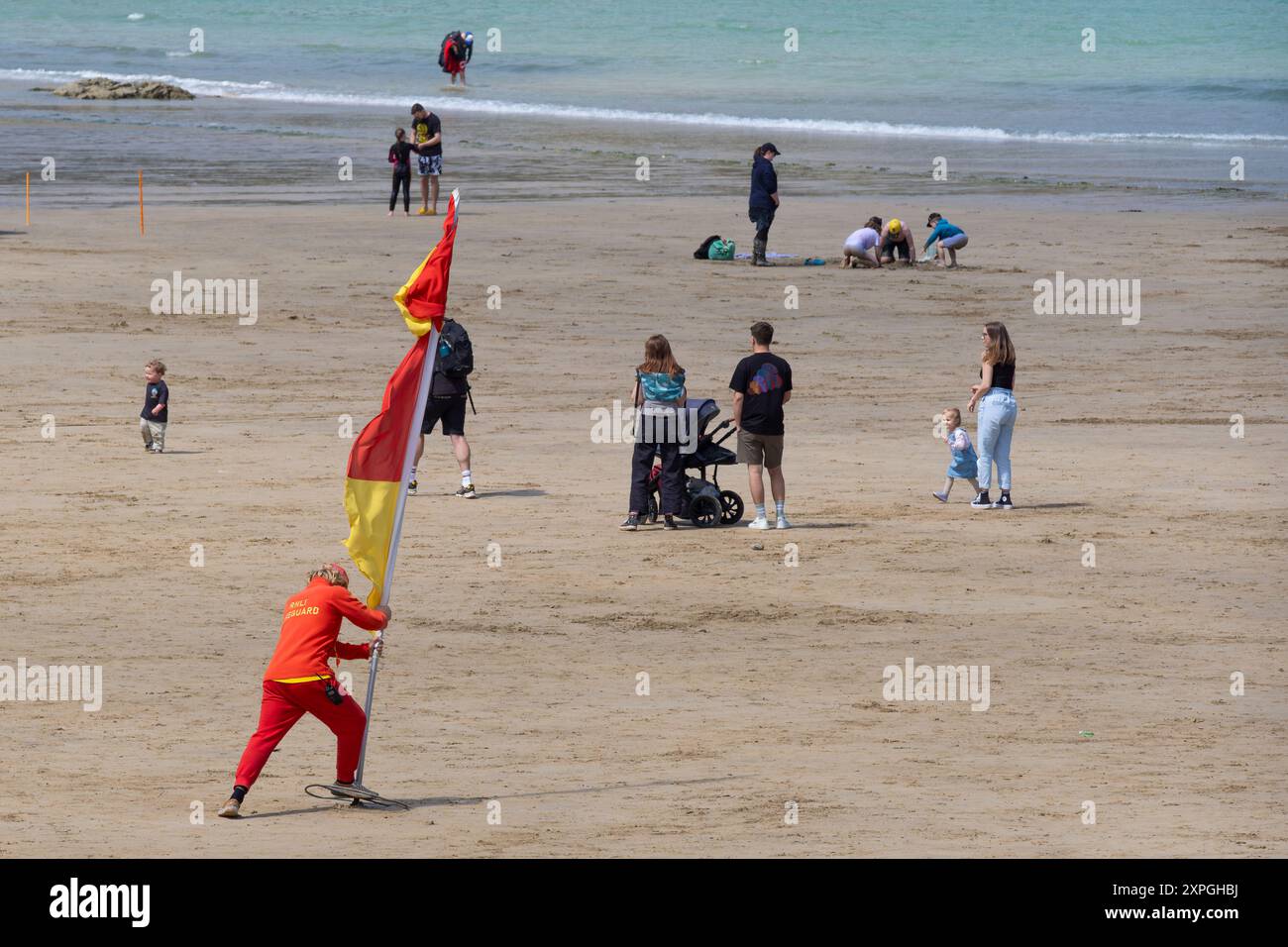 A RNLI Lifeguard setting up a yellow and red safety flag on Towan beach ...