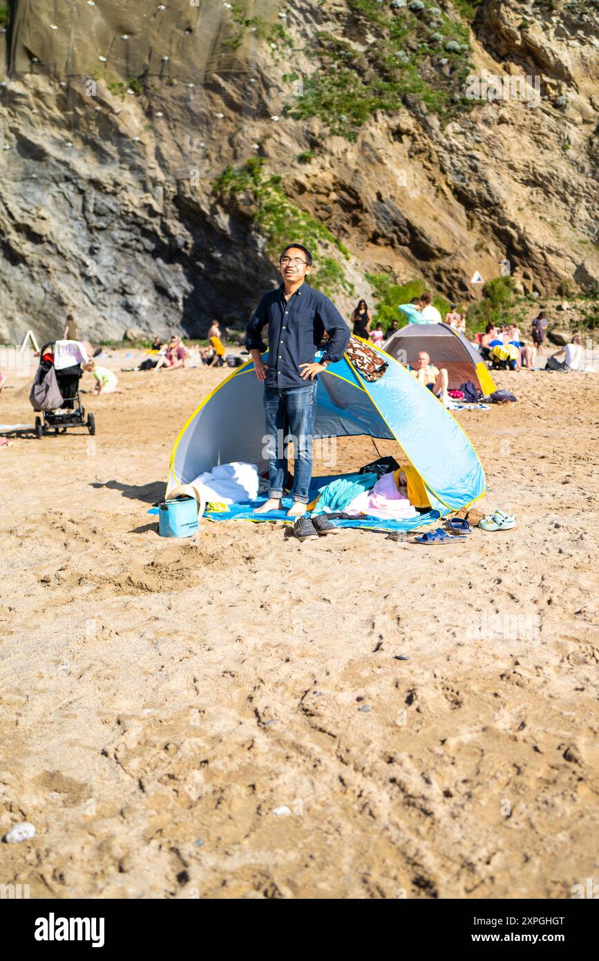 A smiling happy Asian holidaymaker standingby a beach shelter on Gt ...