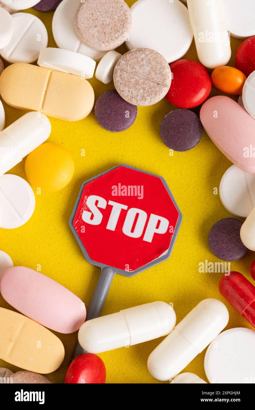 Red stop sign surrounded by many pills and capsules over yellow ...