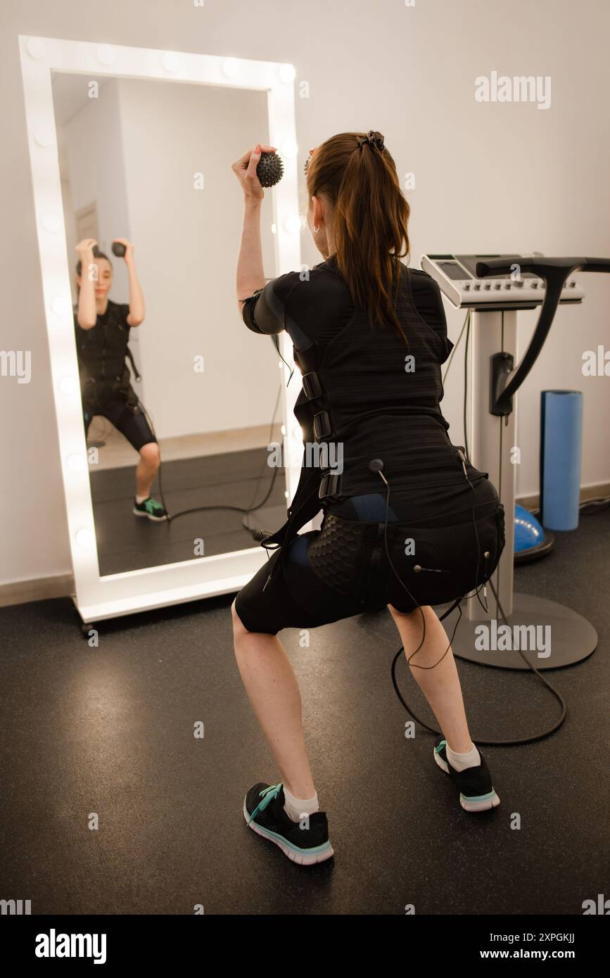 Sporty woman in electrical muscular stimulation suit doing exercise in ...