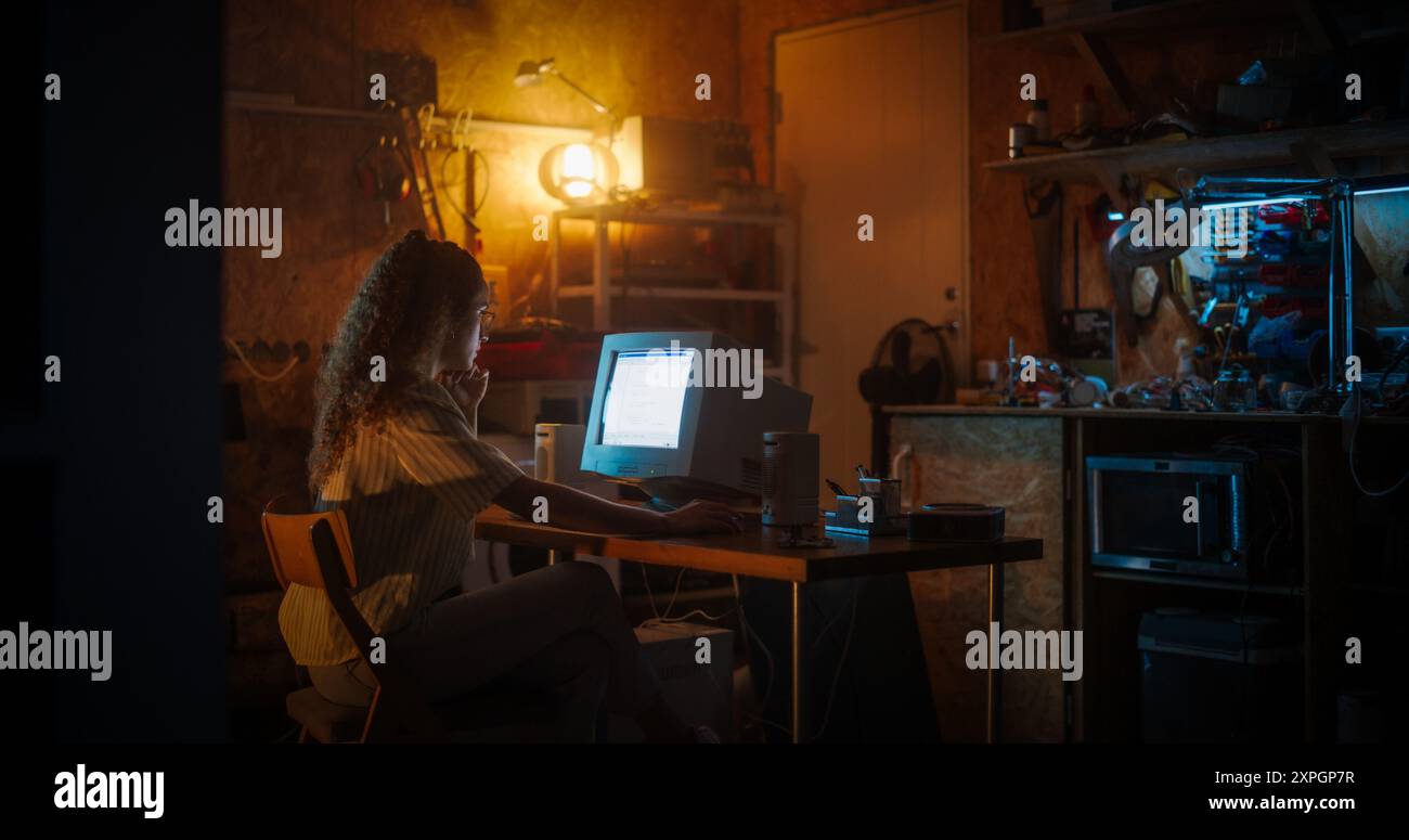 Hispanic Female Web Designer Using Old Desktop Computer In Retro Garage Late At Night. Focused ...