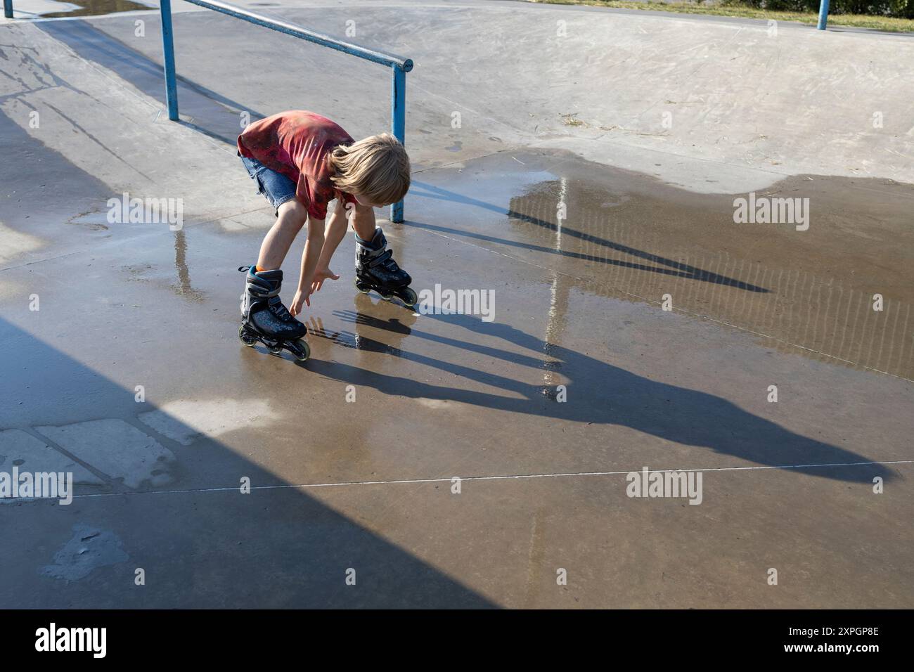 boy joyfully rides on roller skates at speed through puddle on asphalt ...