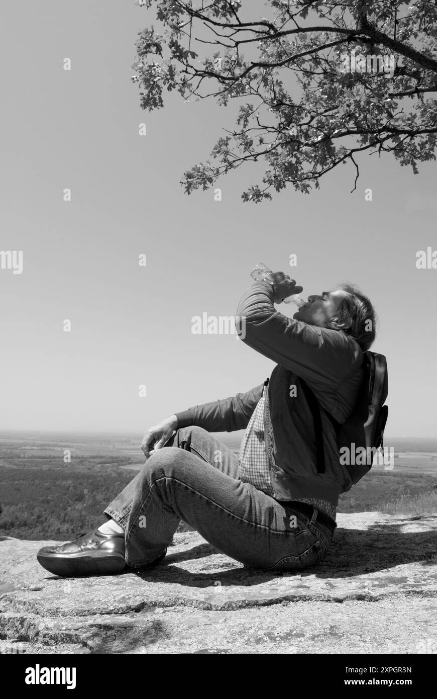Caucasian man, aged 50 to 55, resting and drinking bottled water at an ...