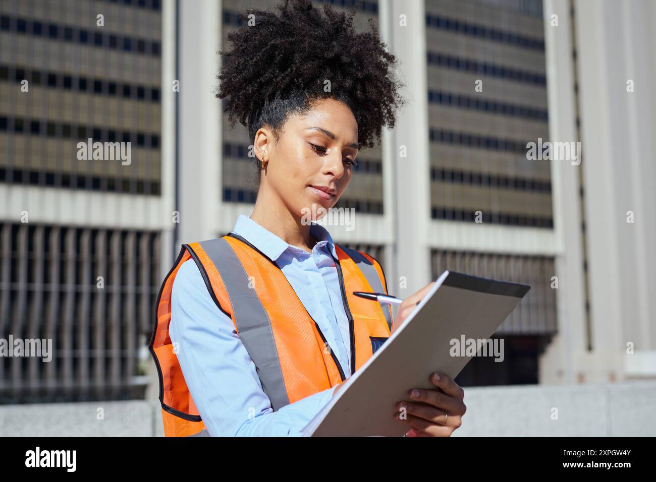 Female Engineer in Safety Vest Inspecting Construction Site with ...