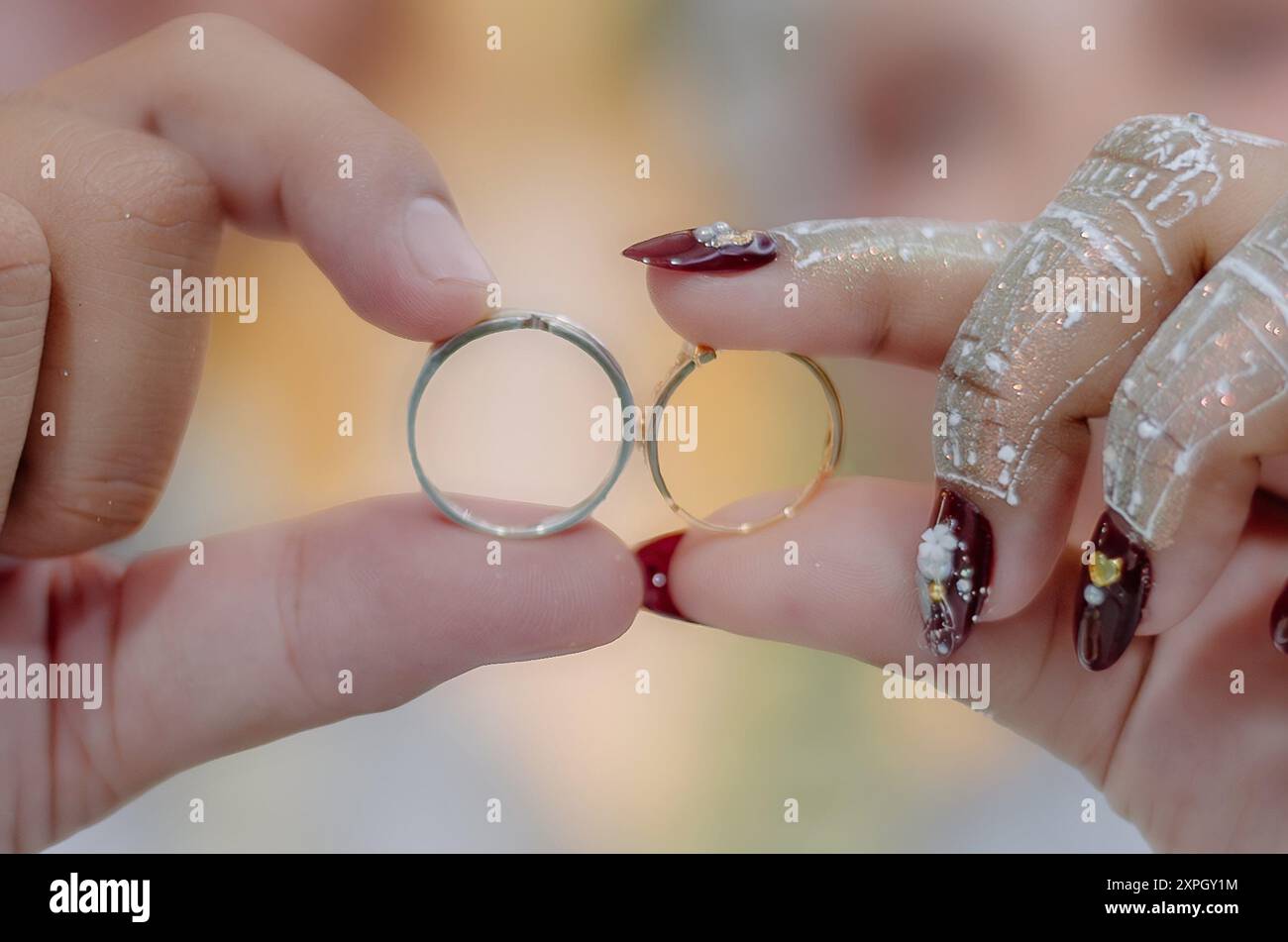 Detailed photo of two gold and silver wedding rings held by the hands of the bride and groom ...