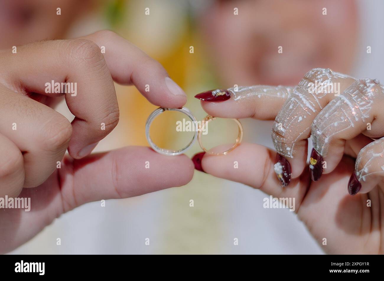 Detailed photo of two gold and silver wedding rings held by the hands of the bride and groom ...