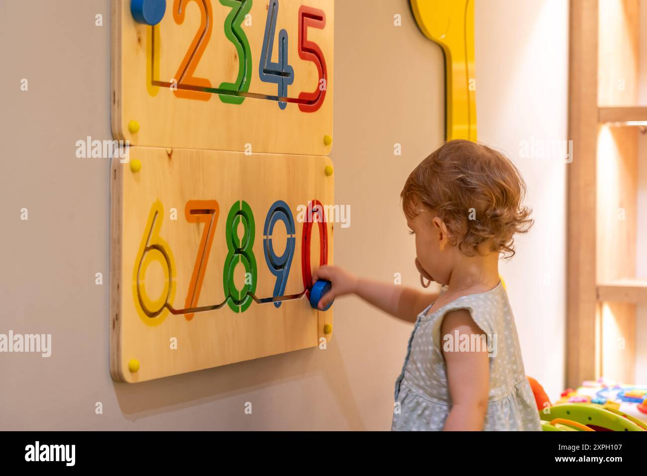 Toddler girl playing with busy board with numbers on the wall ...