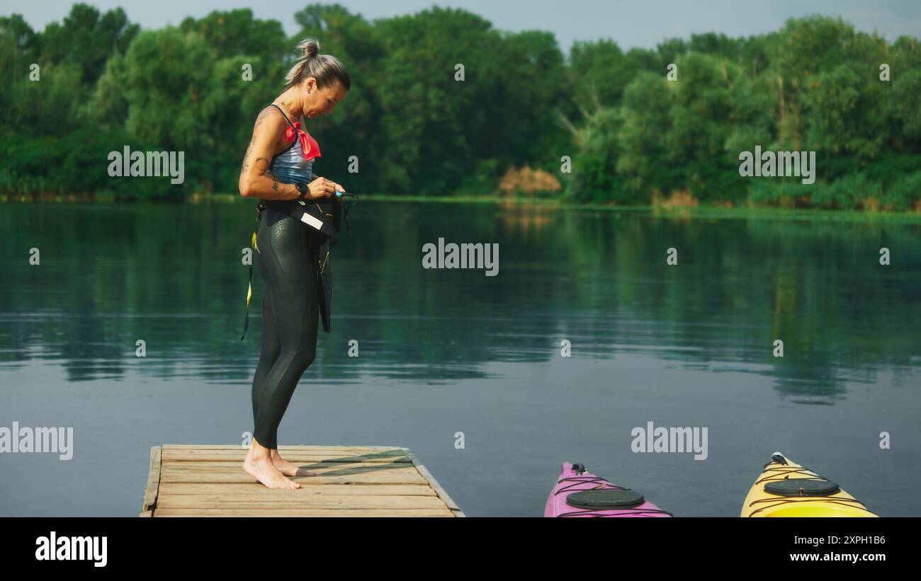 Female swimmer with warms up on dock by calm lake, surrounded by nature ...