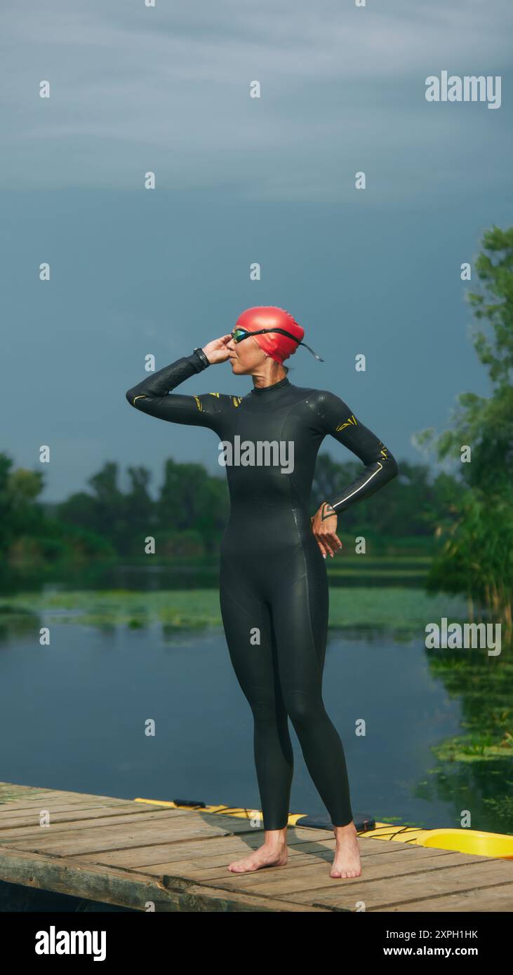 Focused swimmer in wetsuit secures her red swim cap and goggles ...