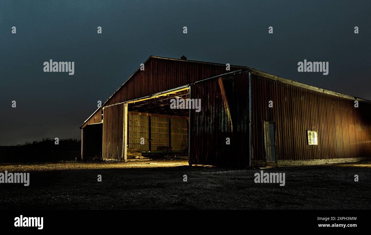 An illuminated wooden barn at night with a dark, cloudy sky in the ...