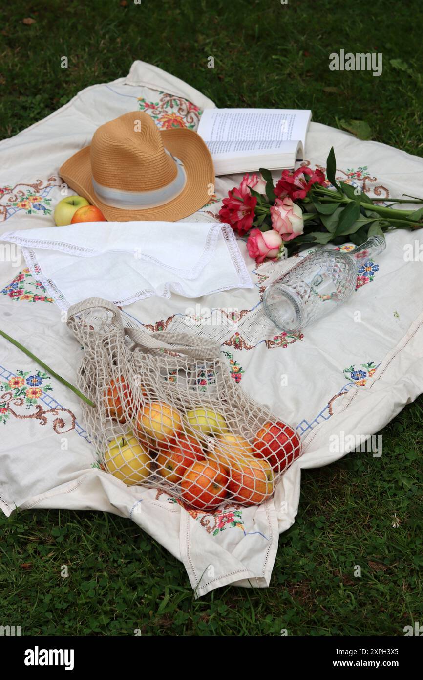 Bouquet of roses, apples, open book and straw hat on a picnic blanket. Summer weekend activities ...