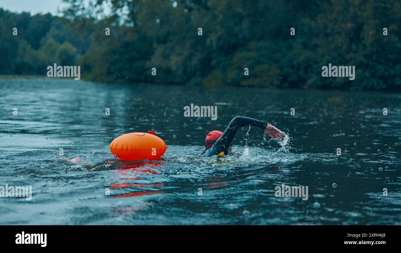 Triathlete in red swim cap and wetsuit powers through training session ...