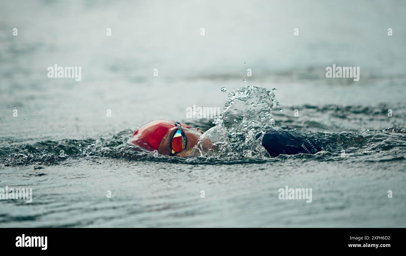 Swimmer in black wetsuit and red cap slices through water, creating ...
