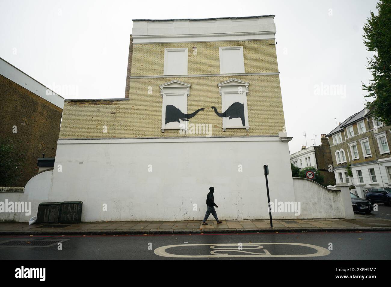 A man passes underneath a new artwork depicting two elephants poking ...