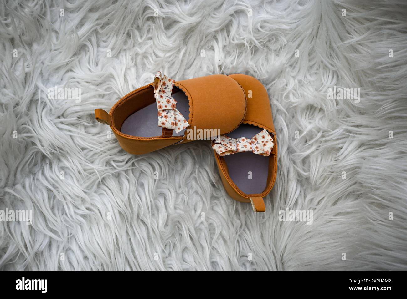 Pair of cute baby girl shoes with a bow is lying on white fur, waiting for the baby to wear ...