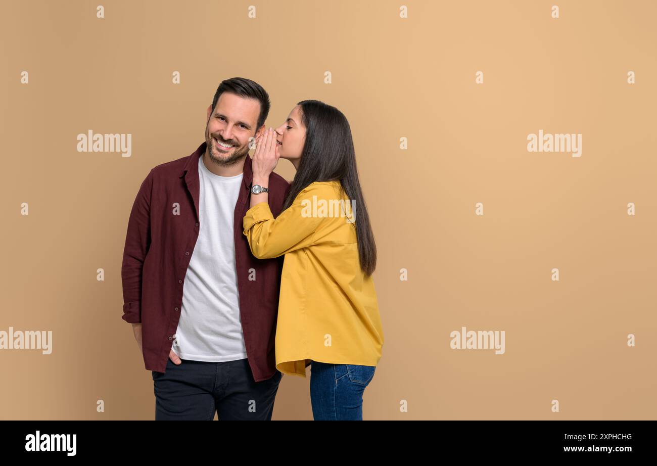 Side view of young woman covering ear of handsome smiling boyfriend ...