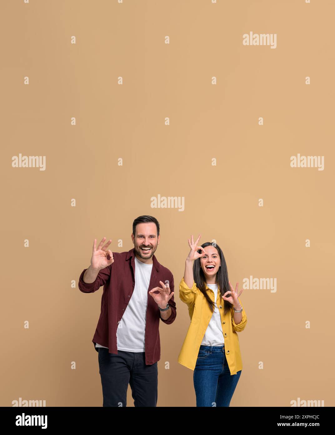 Carefree young couple laughing and showing OK signs while posing ...