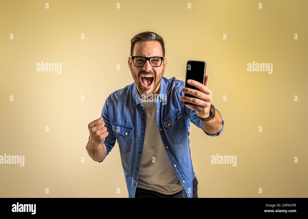 Portrait of cheerful male entrepreneur with smart phone screaming ...