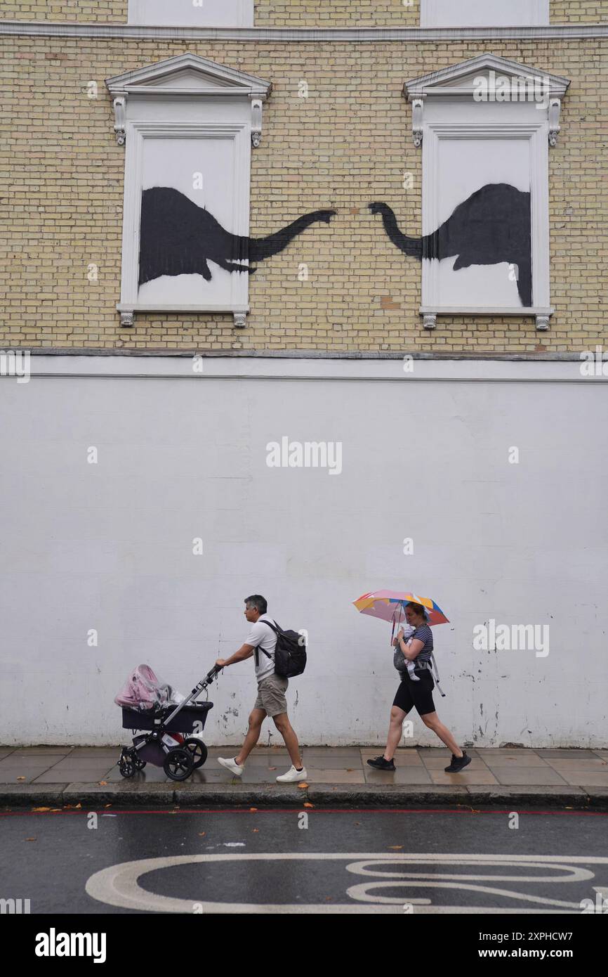 People pass underneath a new artwork depicting two elephants poking ...